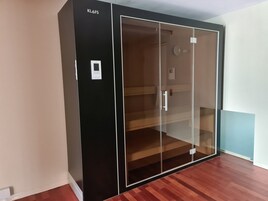 Um guarda-roupa preto com porta de vidro e painel de controle, numa divisão com soalho de madeira e parede de cor clara.