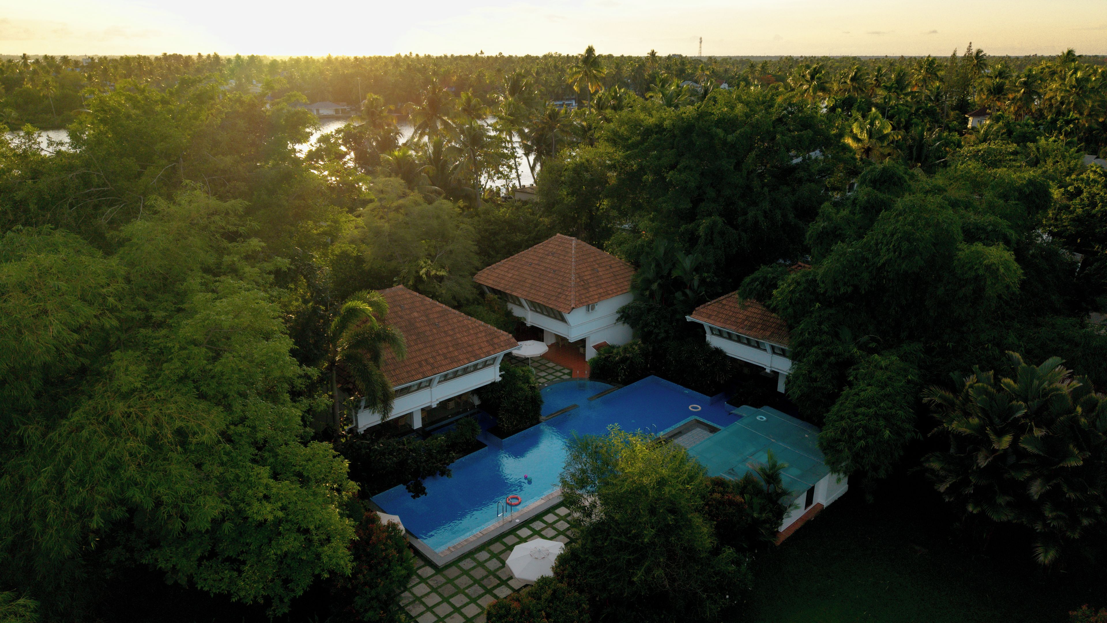 Área residencial com duas casas cercadas por vegetação densa e uma piscina.