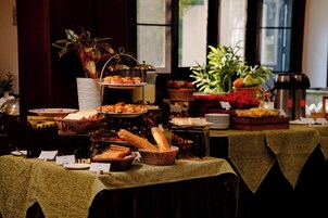 Mesa de buffet com diversos alimentos e uma planta ao fundo.