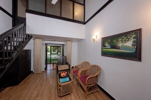 Um quarto amplo com escada, área de jantar com móveis de vime e um quadro na parede.