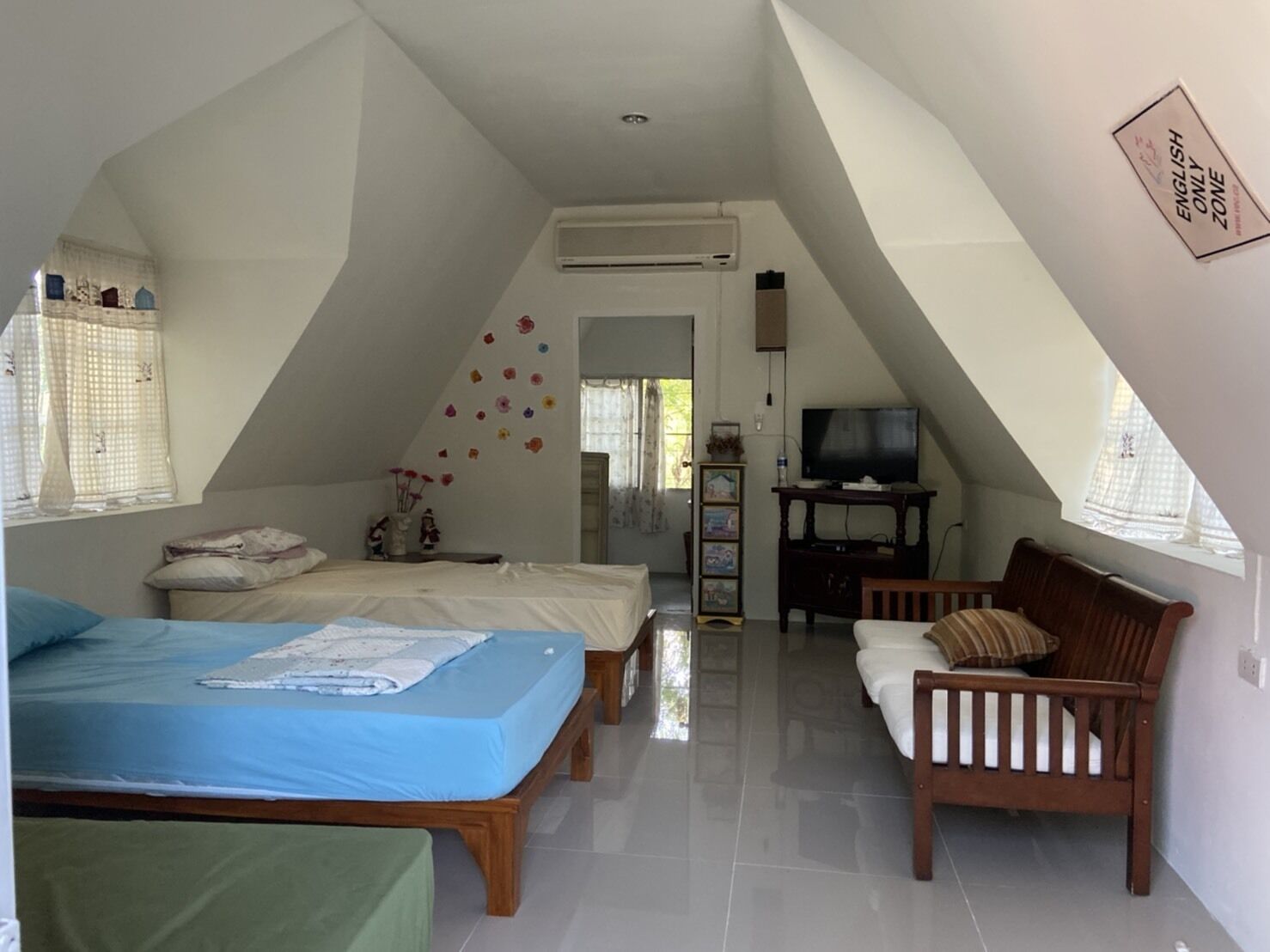 Quarto com duas camas, uma TV e um sofá pequeno.