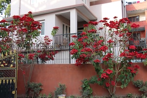 Um edifício com varanda, um portão preto e plantas floridas vermelhas.