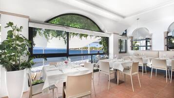 Restaurante com área externa e mesas e cadeiras brancas, com vista para a praia.