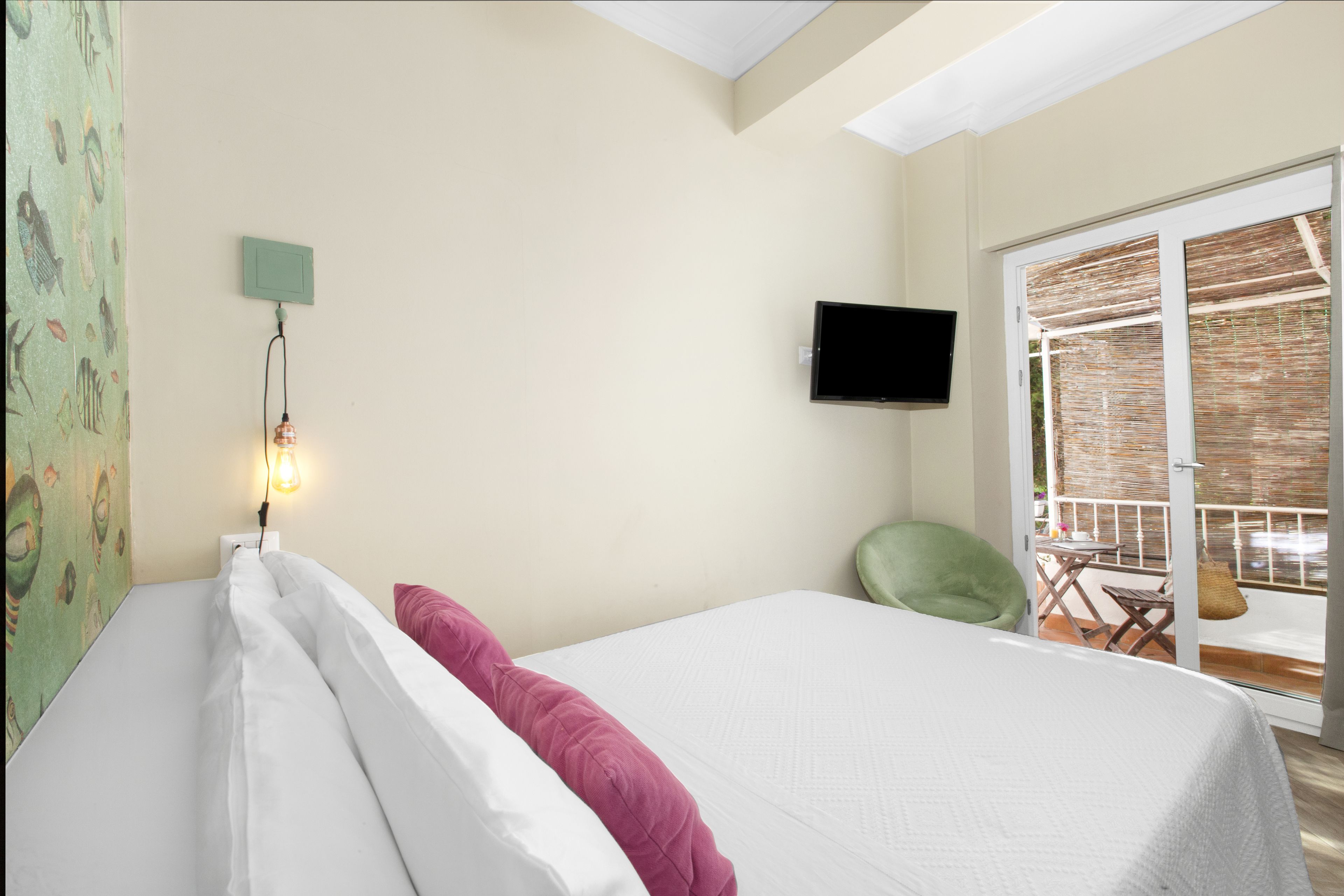 Quarto com cama, televisão fixada na parede e porta de vidro deslizante para área externa.
