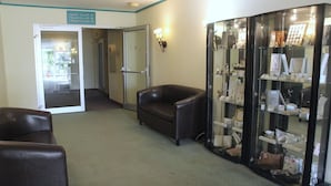 Uma área de recepção com uma vitrine de joias, um sofá de couro marrom e uma porta que dá para outro espaço.