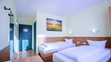 Quarto de hotel com duas camas de solteiro, cabeceira de madeira, pintura de um pôr do sol e uma escrivaninha de madeira.
