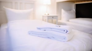 Quarto de hotel com cama bem arrumada, abajur e pequena mesa com luminária.