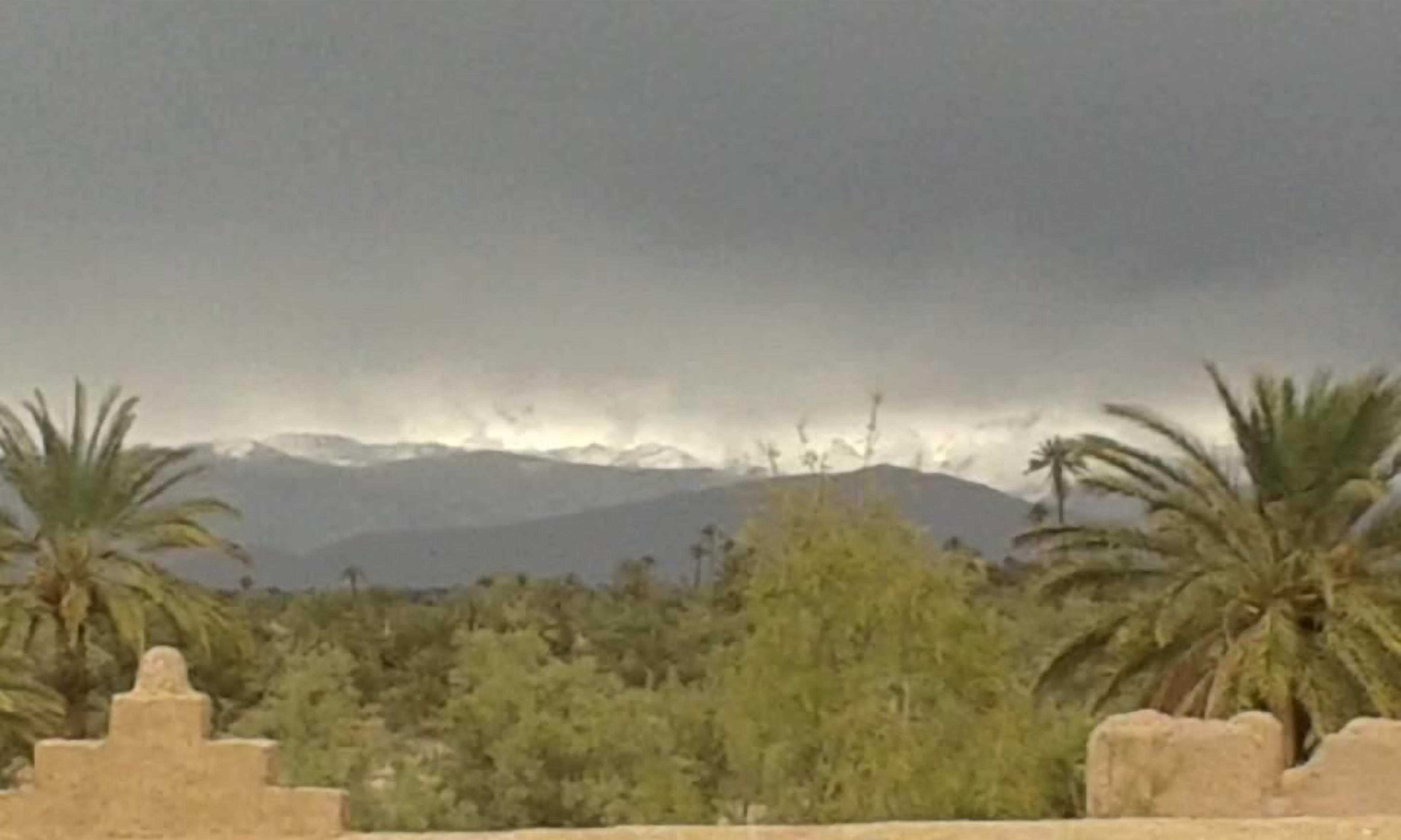 Vista de uma paisagem montanhosa com palmeiras e uma construção de pedra em primeiro plano.