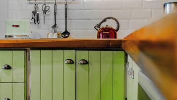 Uma cozinha com armários verdes, uma chaleira e diversos utensílios pendurados na parede.
