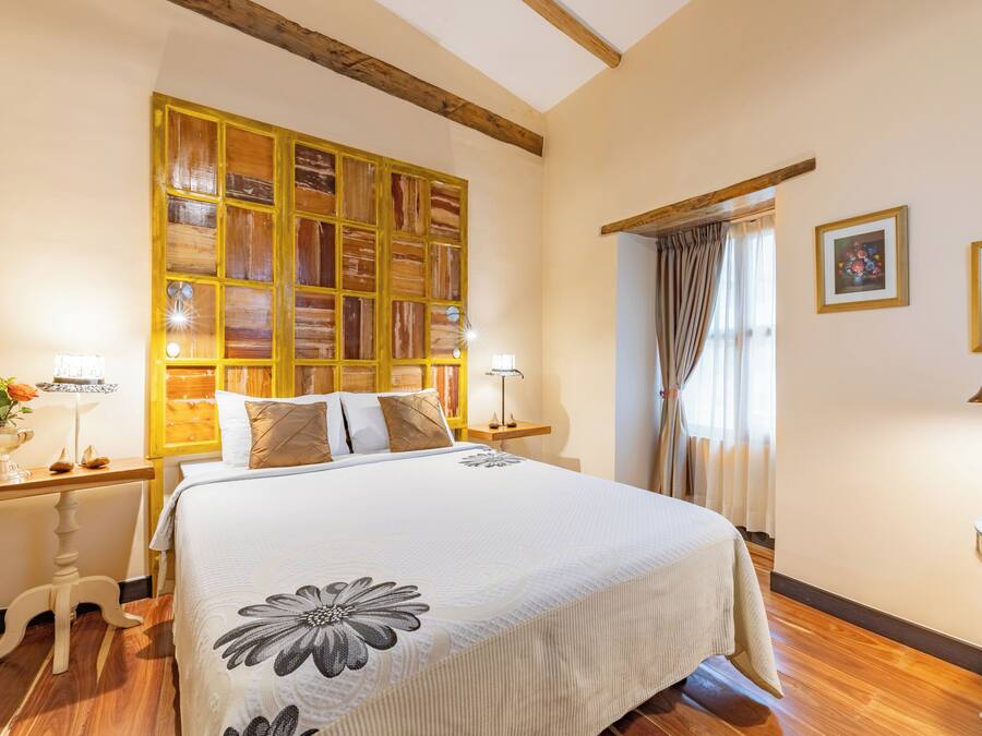 Quarto com cama grande, cabeceira de madeira, mesas de cabeceira e criado-mudo.