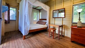 Quarto com cama de dossel, escrivaninha de madeira, cômoda, espelho e ventilador de teto.