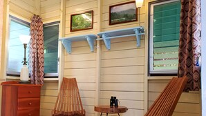 Quarto com paredes de madeira, uma cômoda de madeira, duas cadeiras de madeira, uma pequena mesa com garrafas e quadros nas paredes.