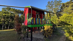 Uma casa vermelha e verde com uma varanda colorida, rodeada por vegetação exuberante.