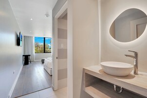 Uma casa de banho moderna com um espelho oval grande, uma sanita branca e uma cómoda de madeira.