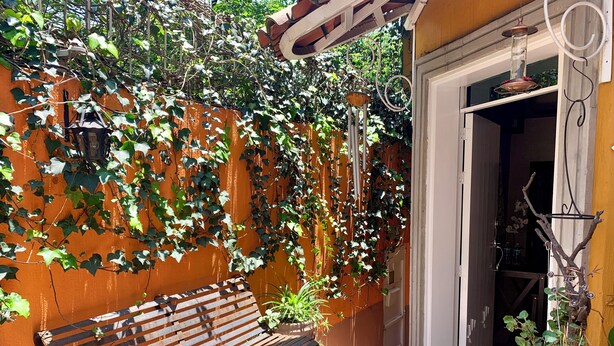 Um banco de madeira, um pátio com azulejos e uma porta de entrada para um quarto com porta branca.