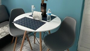 Uma área de refeições com uma mesa redonda, duas cadeiras, um espelho decorativo, um vaso com flores secas e duas garrafas de água.