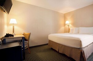 Quarto de hotel com cama, escrivaninha, cadeira, luminárias e televisão.