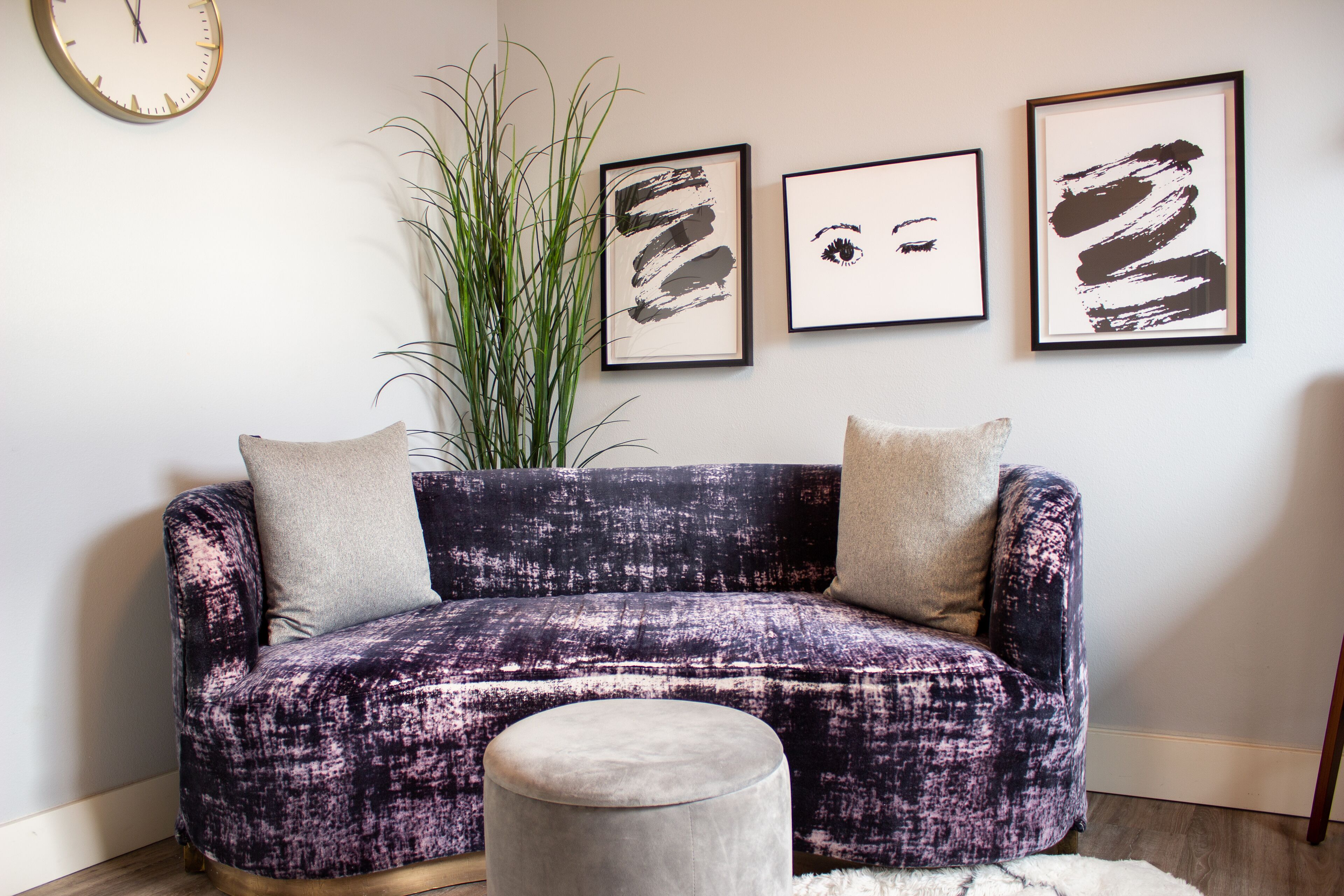 Uma sala de estar moderna com um sofá texturizado roxo e preto, um banquinho redondo e três quadros abstratos na parede.