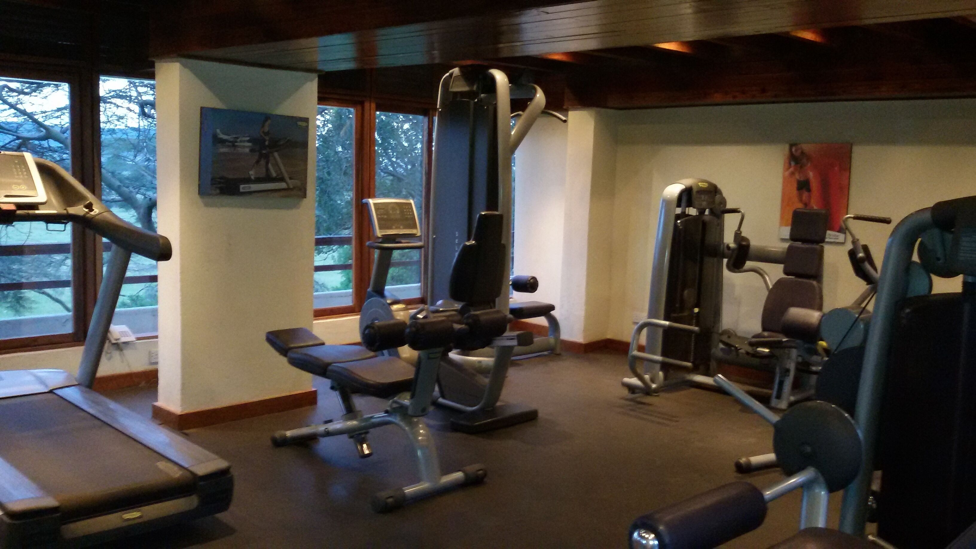 Uma academia com diversos equipamentos de exercício, incluindo esteiras e máquinas de peso, com grandes janelas que oferecem luz natural.