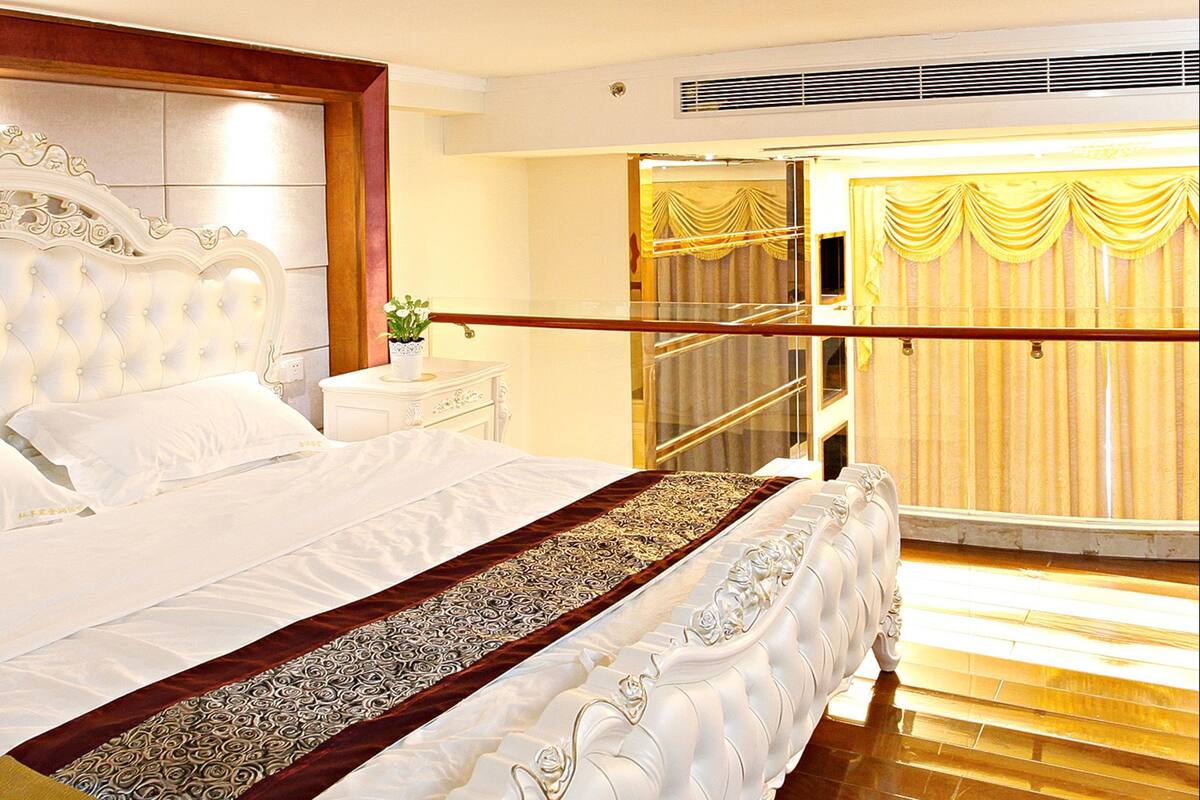 Uma cama grande e ricamente decorada, com alta cabeceira e um corredor decorativo.