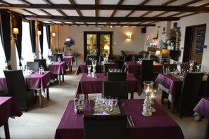 Um restaurante com várias mesas preparadas para refeições, apresentando um interior tradicional com vigas de madeira aparentes e um ambiente acolhedor.