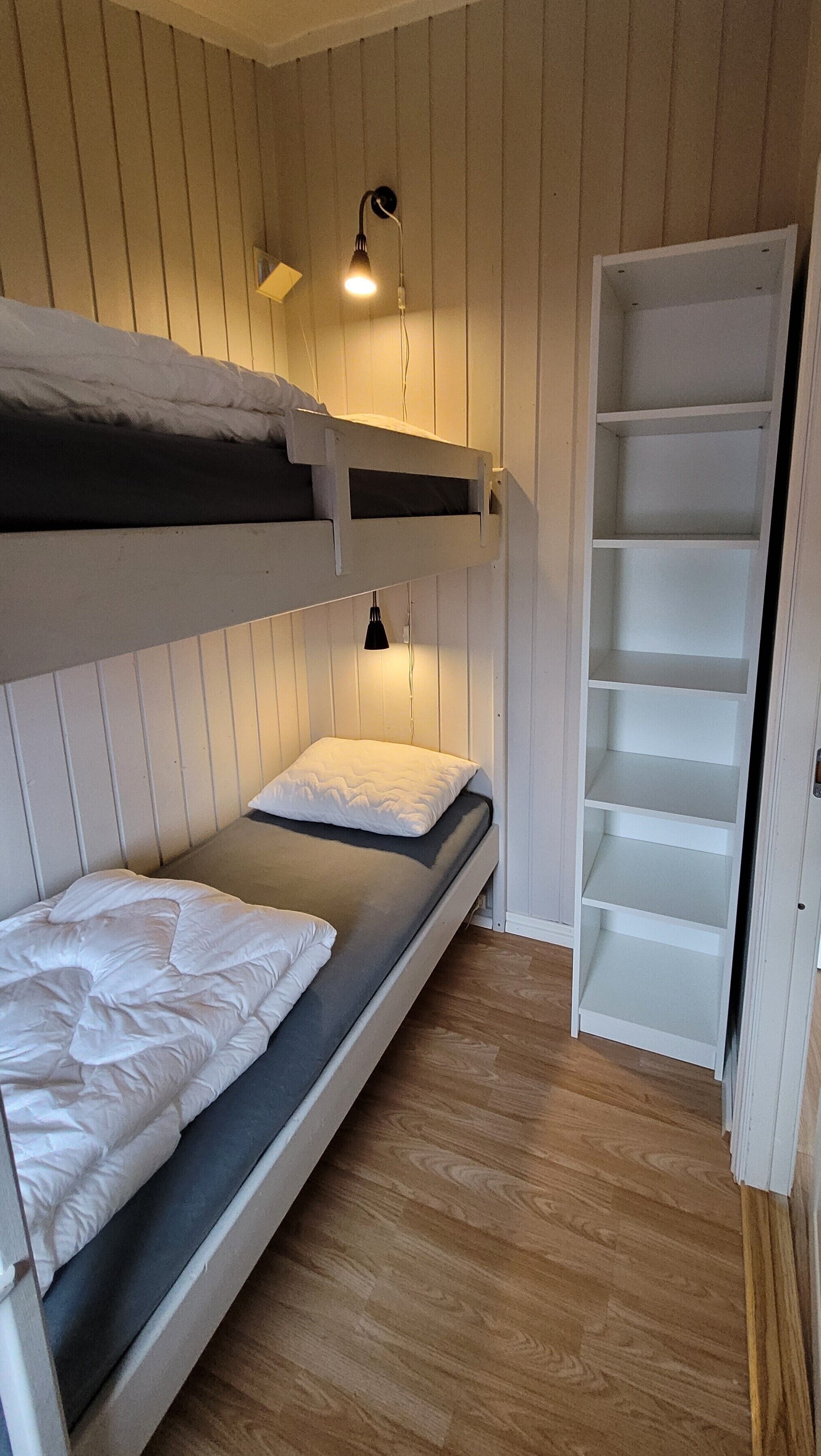 Quarto pequeno e compacto com beliches, um guarda-roupa branco e uma pequena escrivaninha.
