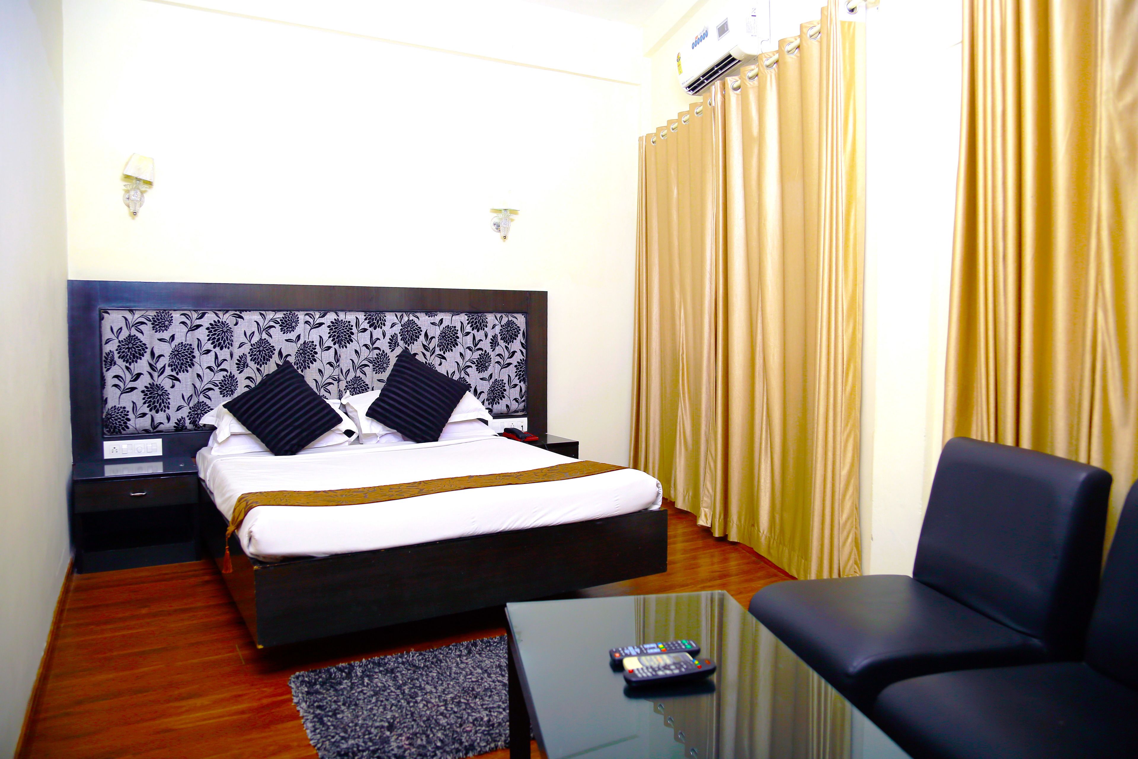 Quarto de hotel com cama, mesa de cabeceira, cadeira e uma pequena mesa com controle remoto.