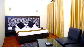 Quarto de hotel com cama, mesa de cabeceira, cadeira e uma pequena mesa com controle remoto.