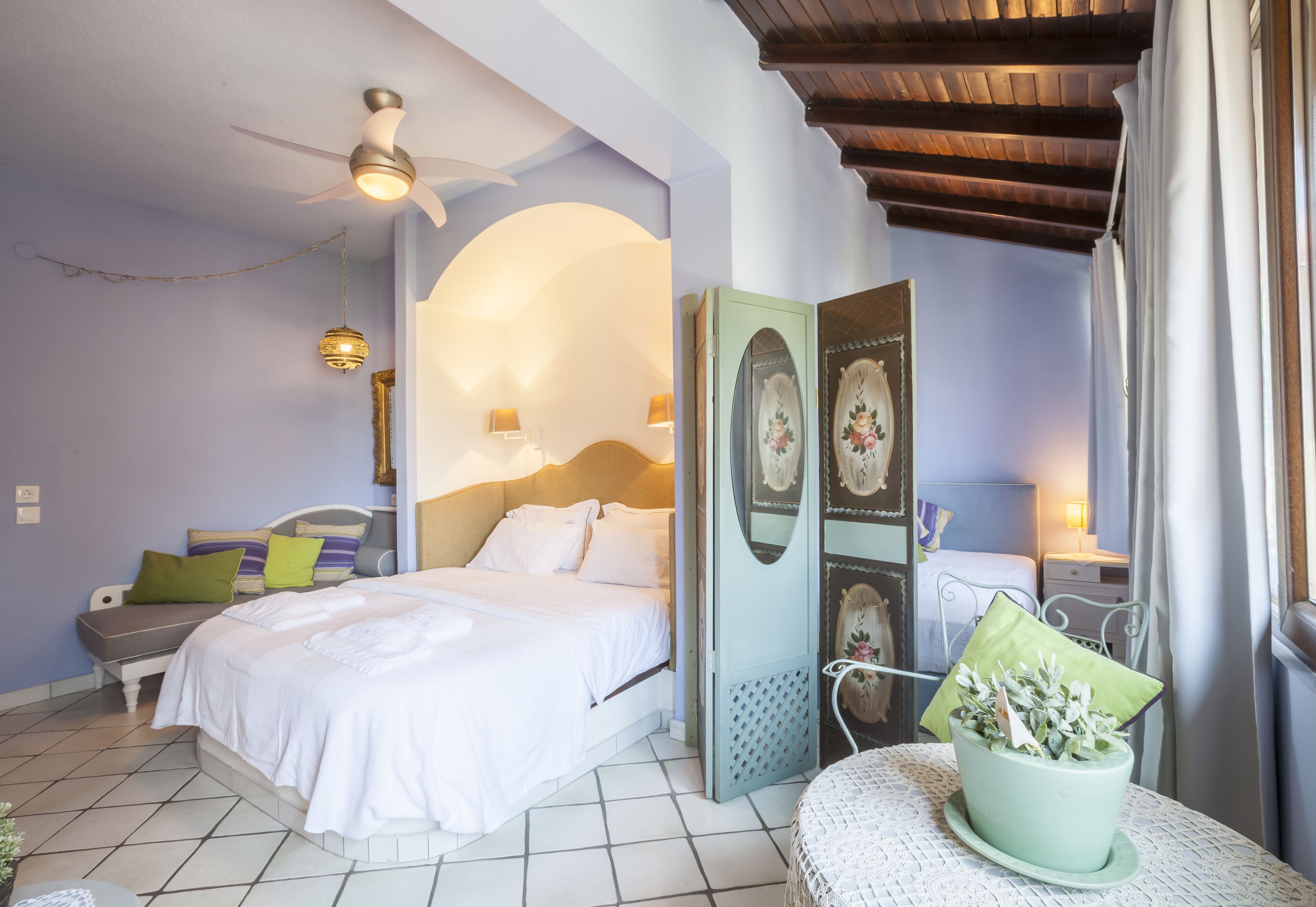 Quarto com cama, mesas de cabeceira, ventoinha no teto e painel decorativo na parede.