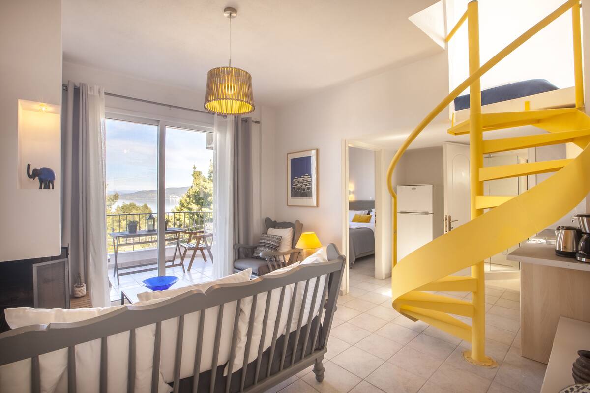 Uma sala de estar ampla com uma escada espiral amarela moderna, uma varanda com vista e uma área de estar aconchegante.