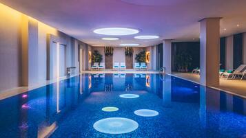 Uma piscina interior moderna com água azul cristalina, iluminação embutida e espreguiçadeiras ao longo das bordas.