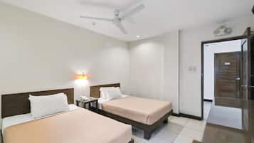 Quarto de hotel com duas camas, um ventilador de teto, uma mesa de cabeceira com abajur e uma porta com o número 403.
