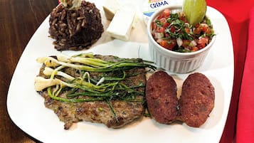 Um prato com bife, duas hambúrgueres, acompanhamento de arroz, uma fatia de pão e uma tigela de salada.