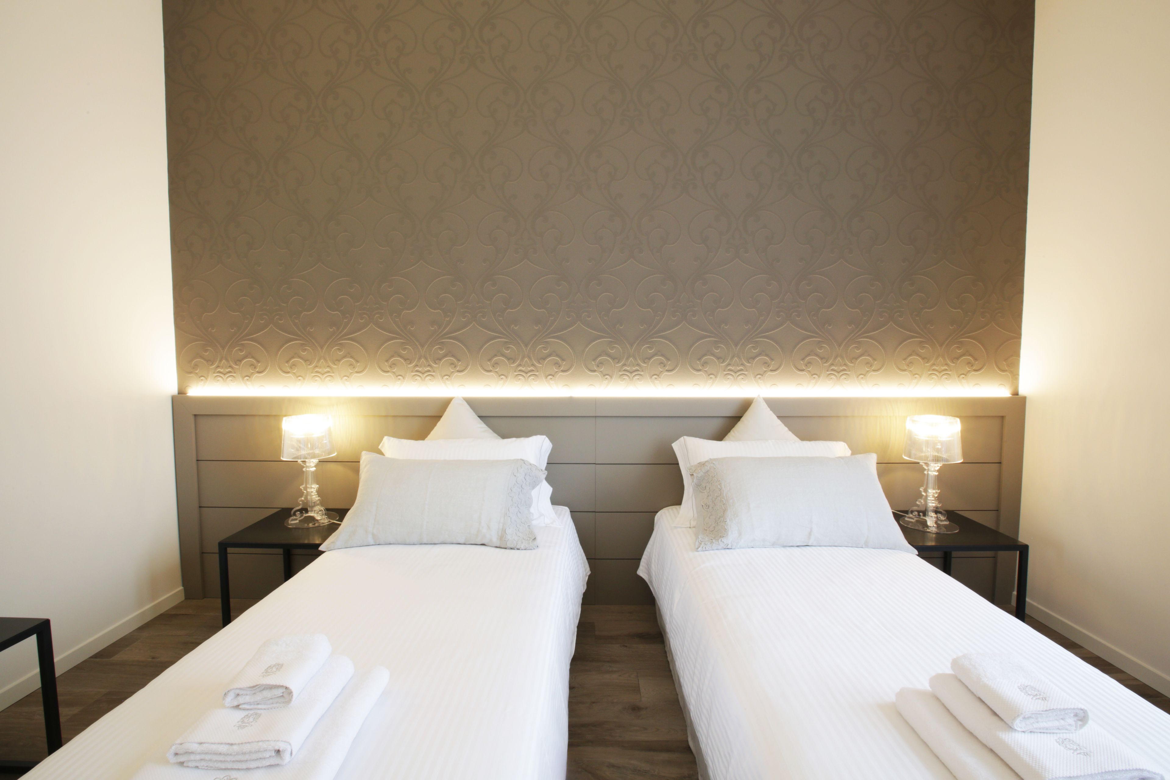 Quarto de hotel com duas camas de solteiro, cada uma com uma mesa de cabeceira, uma luminária e toalhas dobradas com cuidado.