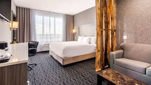 Quarto de hotel com cama, escrivaninha, poltrona, sofá e uma janela grande com cortinas.