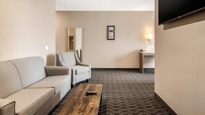 Quarto de hotel com sofá, poltrona e mesa de centro de madeira.