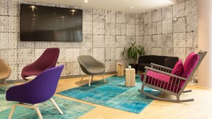 Uma sala de estar moderna com televisão de tela plana, papel de parede estampado e diversas opções de assento, incluindo uma cadeira de balanço e poltronas.