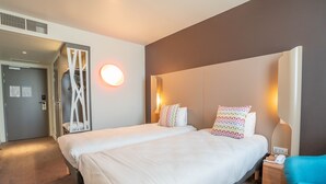 Quarto de hotel com cama grande, mesas de cabeceira, uma cadeira e luminária na parede.