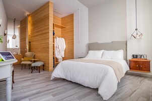 Quarto moderno com uma cama grande, lambris de madeira, um espaço de estar pequeno e uma mesa com um tablet.