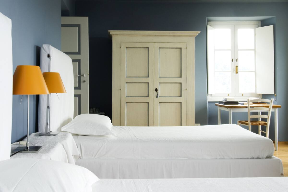 Quarto de hotel com duas camas, uma escrivaninha, uma cadeira e um guarda-roupa.