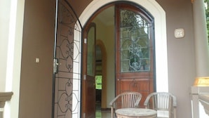 Uma entrada ampla com uma grande porta em arco, um portão de metal decorativo e uma pequena mesa redonda com duas cadeiras.