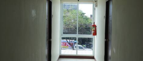 Um corredor com porta de vidro que dá para o exterior, um extintor de incêndio na parede e uma saída de ventilação no teto.