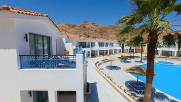 Resort com piscina, palmeiras e montanhas ao fundo.