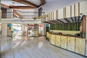 Um hall espaçoso com piso de mármore, um balcão de recepção, uma escadaria e vista para o exterior.