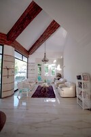 Uma sala de estar espaçosa com móveis brancos, uma janela grande e teto de madeira.