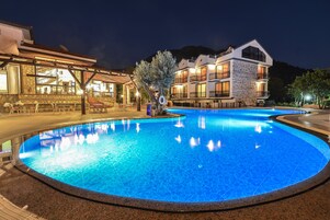 Piscina com borda de pedra, um edifício com varandas e uma montanha ao fundo.