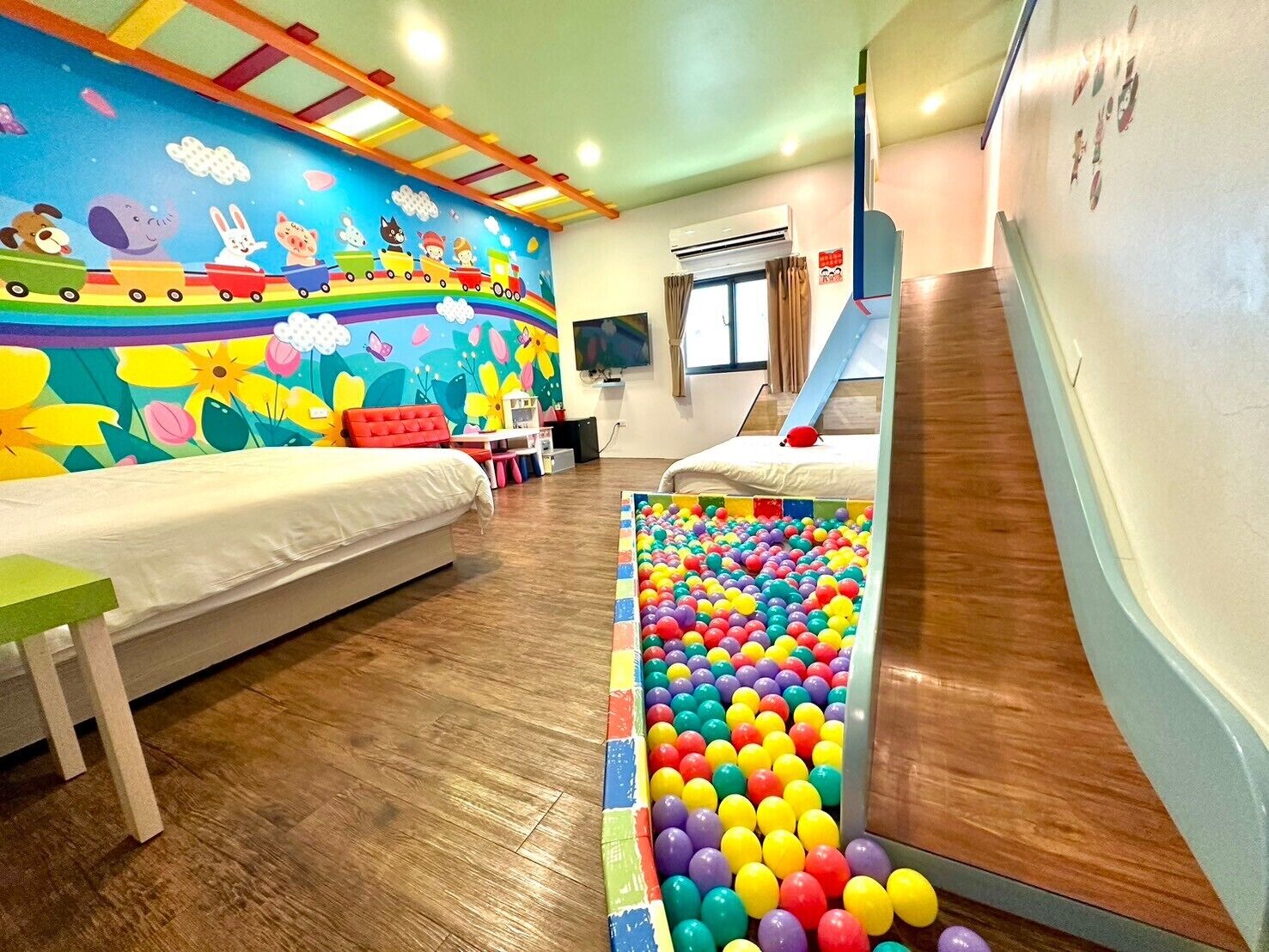 Um espaço infantil com uma piscina de bolinhas colorida, beliches e um mural com animais e um arco-íris.