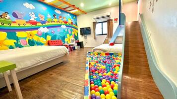 Um espaço infantil com uma piscina de bolinhas colorida, beliches e um mural com animais e um arco-íris.