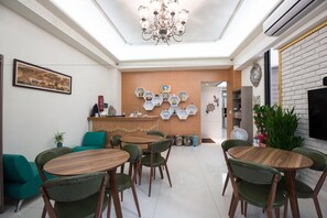 Uma área de refeições moderna com mesa de madeira e cadeiras verdes, um balcão de recepção com prateleiras hexagonais e uma parede decorativa.