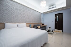 Quarto de hotel moderno com uma cama grande, um sofá pequeno, uma escrivaninha com cadeira e uma porta.